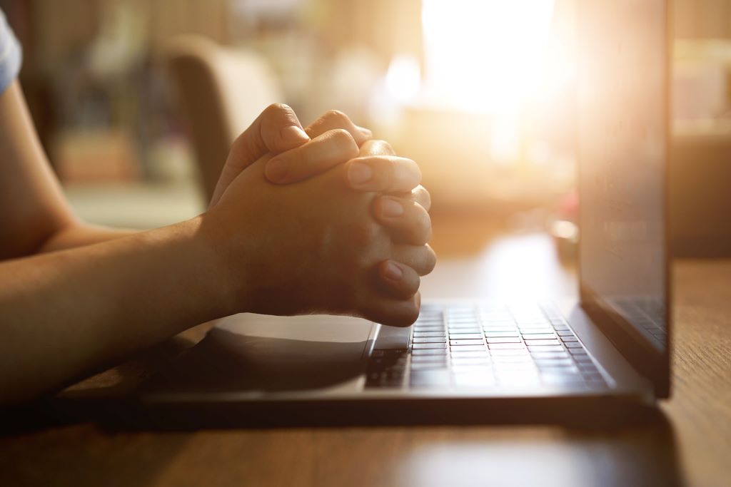 Hands clasped at computer screen with sun shining through the window